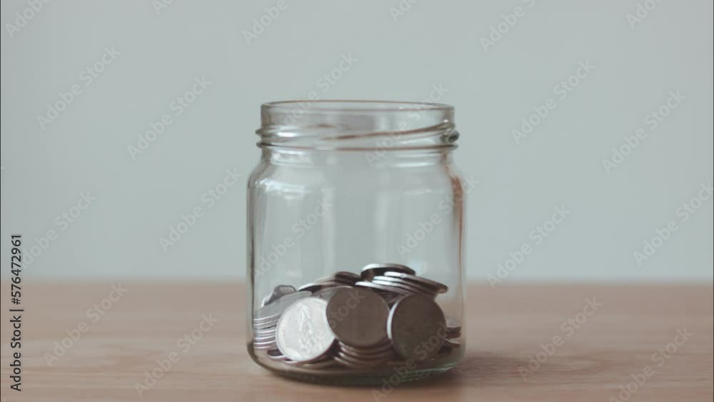 Stop motion animation of rising coins in a clear glass jar on a wooden ...