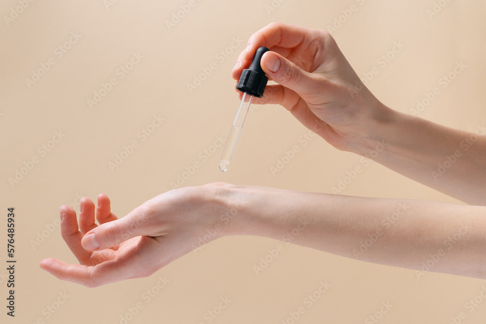 Female hand applying serum from pipette to her wrist on beige isolated ...