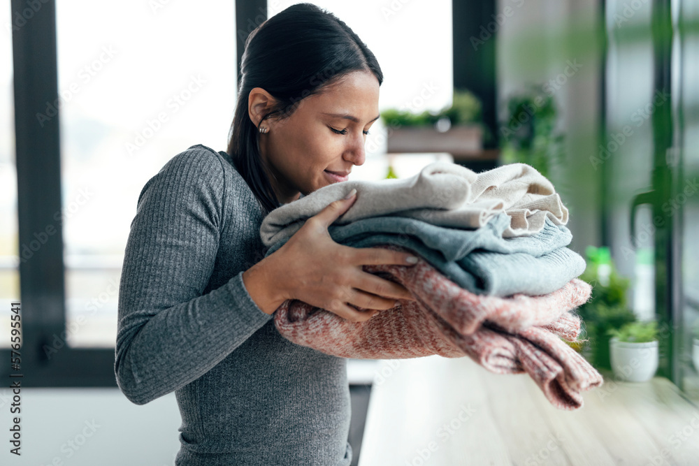 Beautiful young woman holding and smelling clean clothes at home. Stock ...