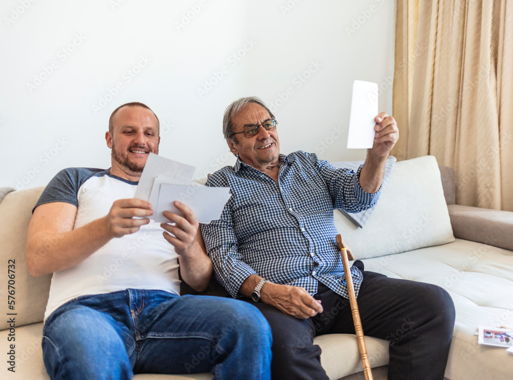 Senior father shows his adult son old photos of his father from younger ...