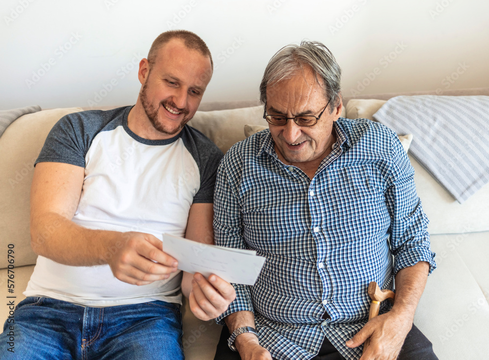 Father and son going through the family album together. Adult son and his father looking through ...