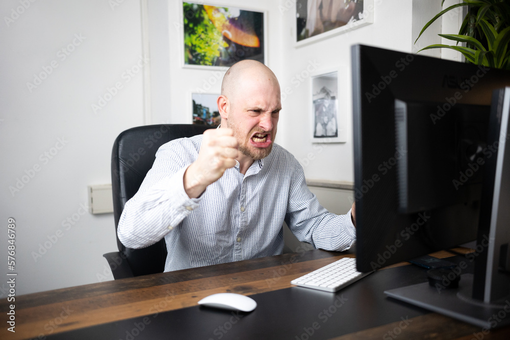 Angry employee with bald head sits screaming with clenched fists in ...