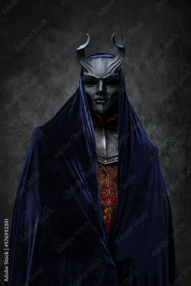 Shot of dark cult prayer dressed in robe and evil mask against dark ...