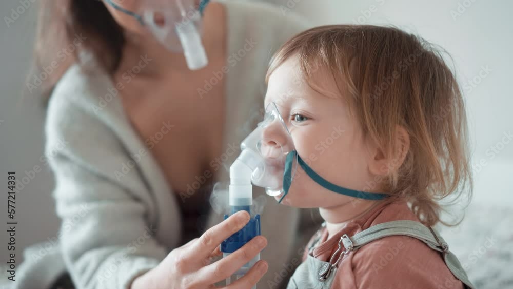 Asian mother helping sick daughter use nebulizer while embracing her on ...