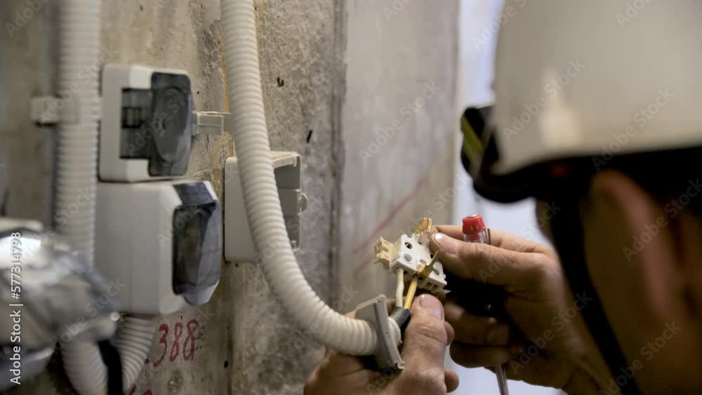 Electrician installs socket to corrugated cable near concrete wall ...