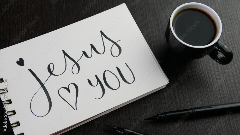 JESUS LOVES YOU with heart symbol lettering in notebook with cup of ...