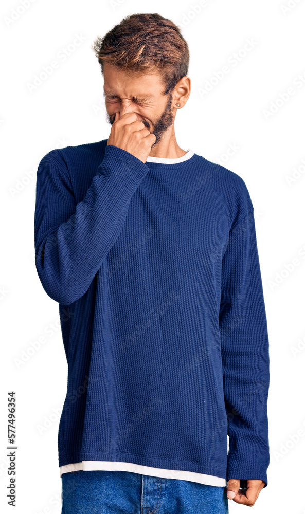 Handsome blond man with beard wearing casual sweater smelling something ...