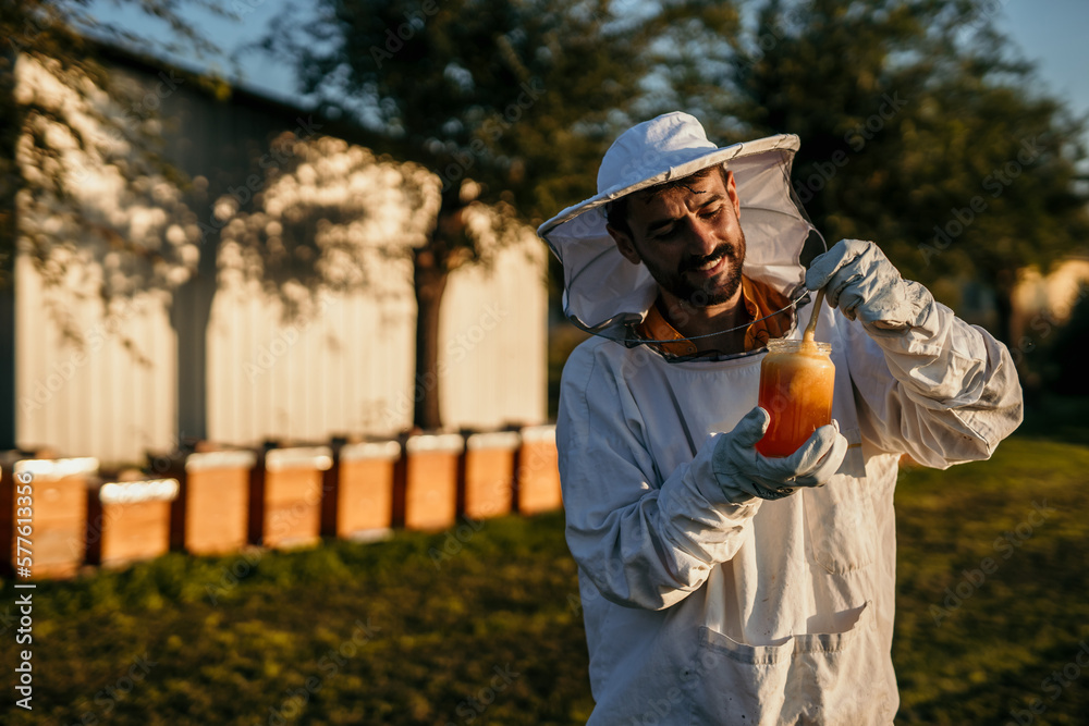 A beekeeper man in his 30s is holding a glass of high-quality bee honey ...