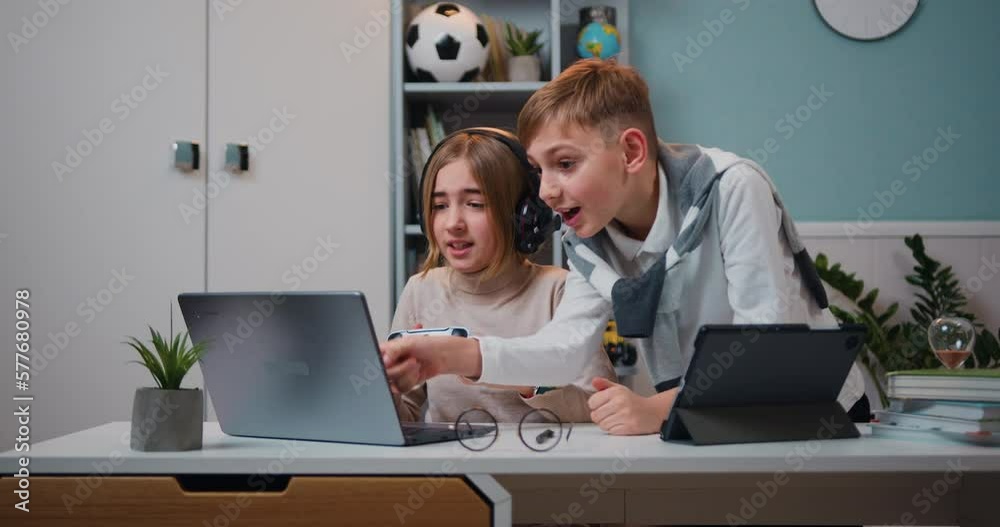 Excited caucasian gamer girl and young boy sitting by table and playing ...