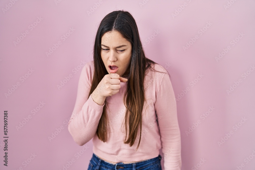 Young brunette woman standing over pink background feeling unwell and ...