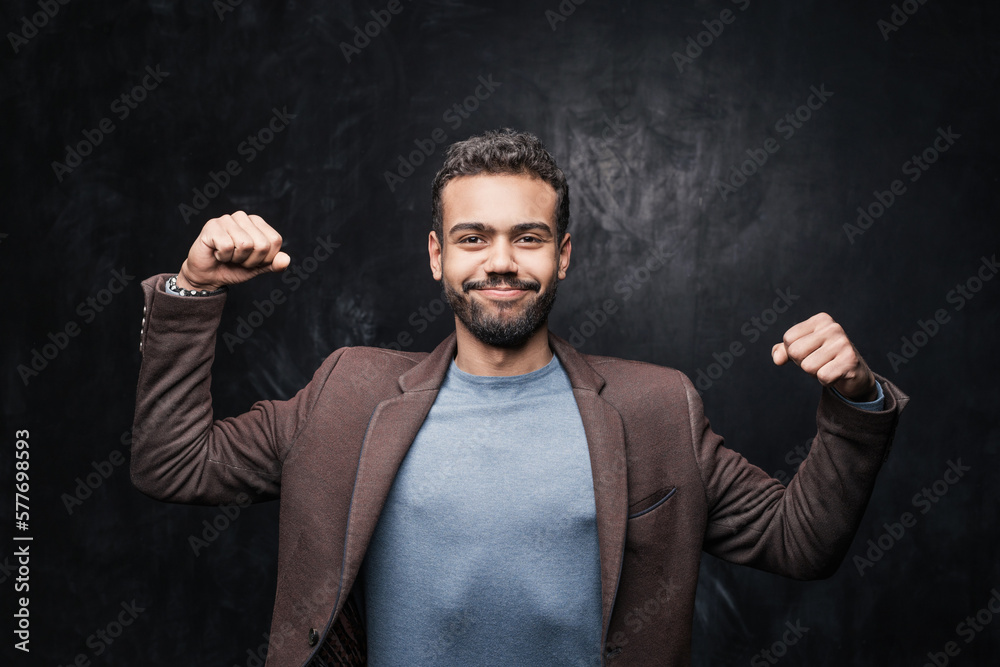 Handsome smiling young man showing strength over black background ...