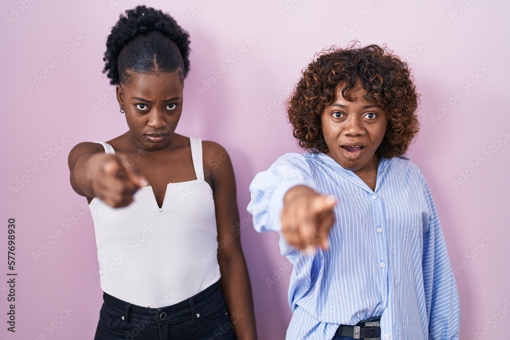 Two african women standing over pink background pointing displeased and ...