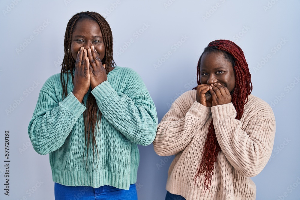 Two african woman standing over blue background laughing and ...