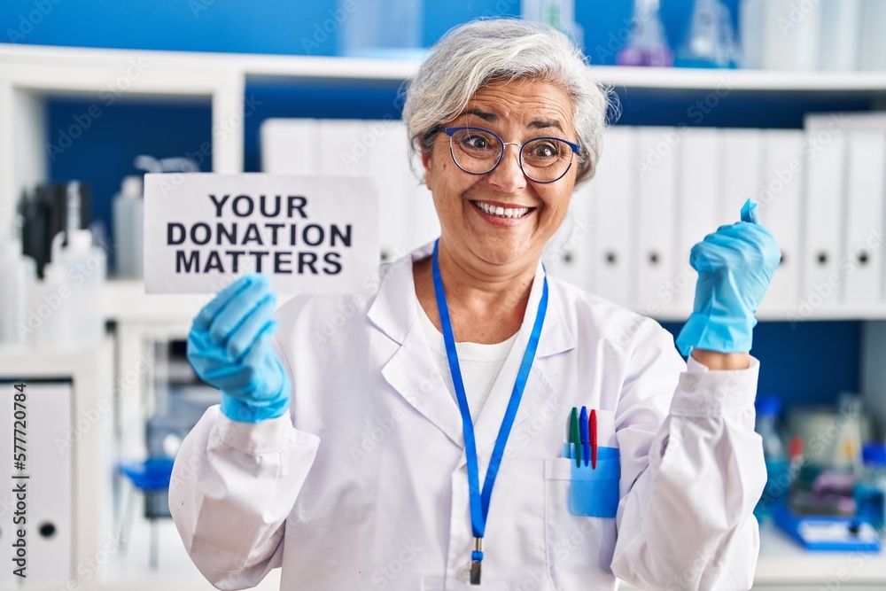 Middle age woman with grey hair working at scientist laboratory holding your donation matters ...