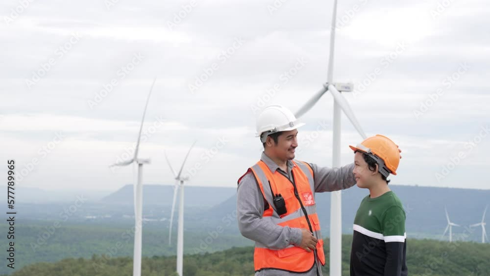 Engineer with his son on a wind farm atop a hill or mountain in the ...