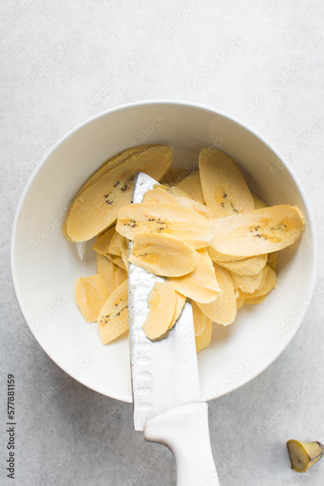 slices of ripe plantains in a white bowl, slices of yellow plantains ...
