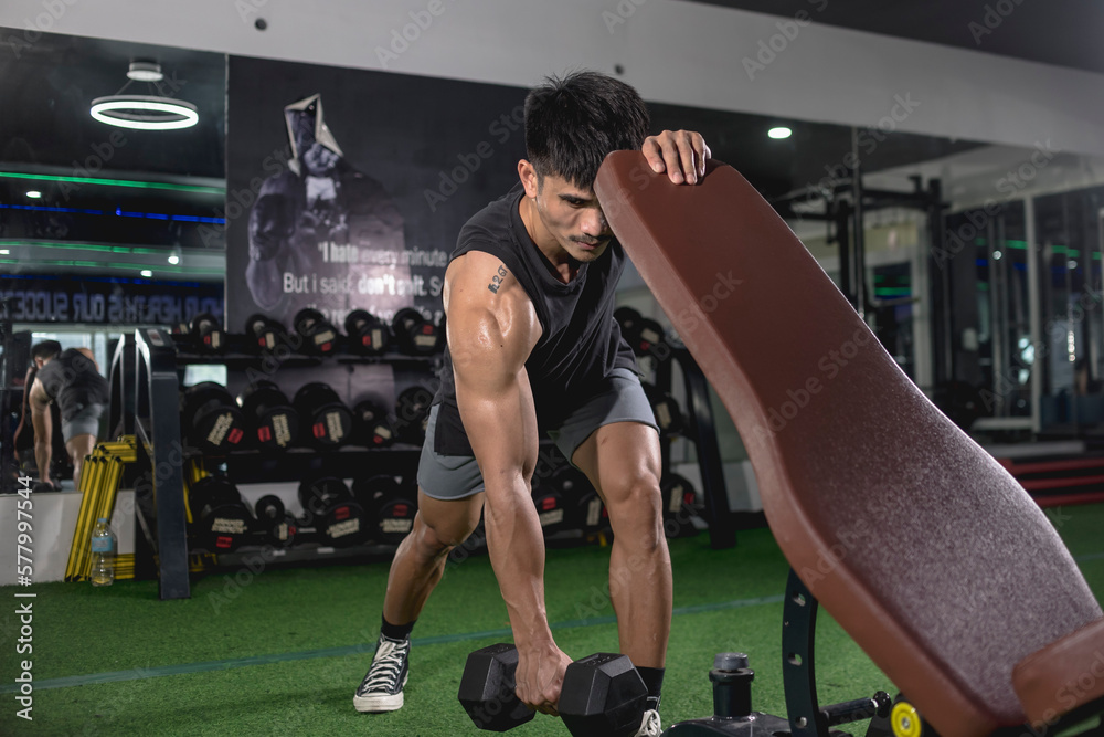 A determined man does one-arm dumbbell rows while leaning on an incline ...
