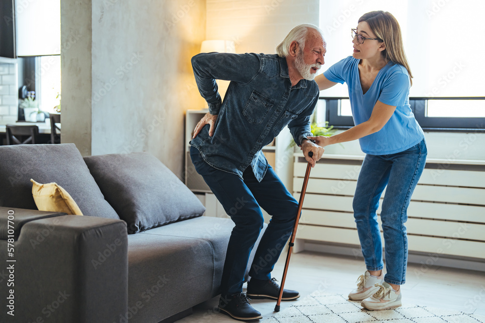Smiling nurse assisting senior man to get up from bed. Caring nurse supporting patient while ...