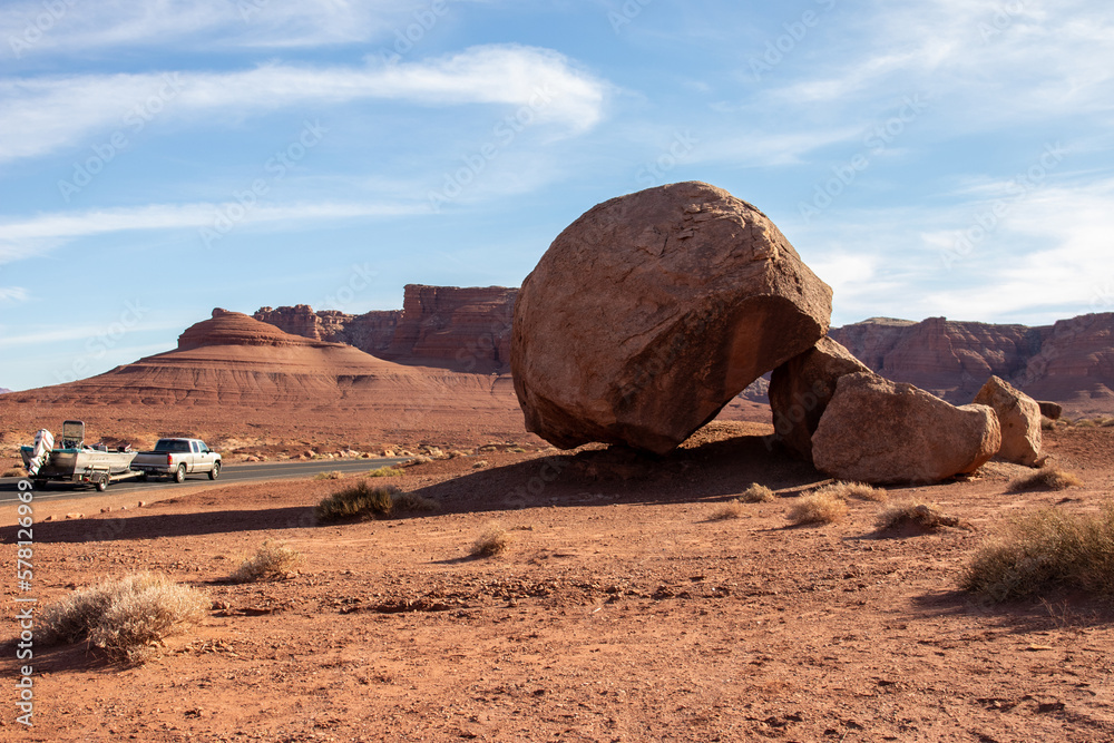 Balanced rock next to a road with a pick up car towing a boat, red ...