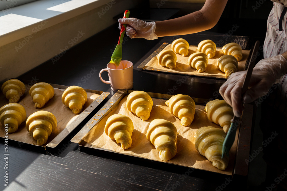 The baker brushes raw formed croissants with egg yolk before baking ...