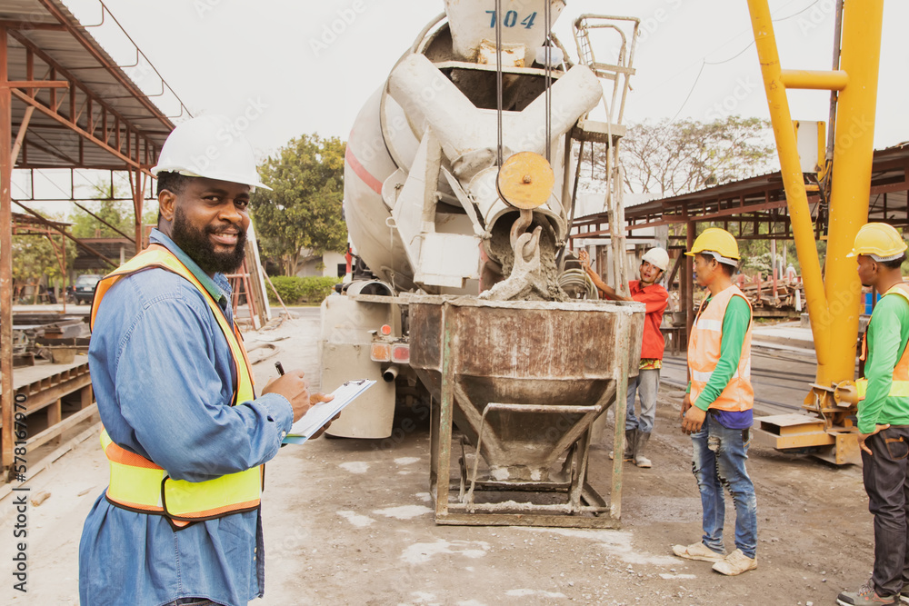 Foto de African American foreman inspects the pouring of mortar from a ...
