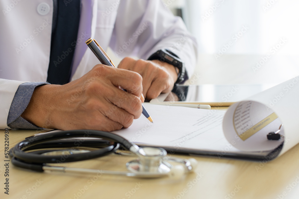 Doctor hand writing on clipboard, with stethoscope on the wooden desk ...