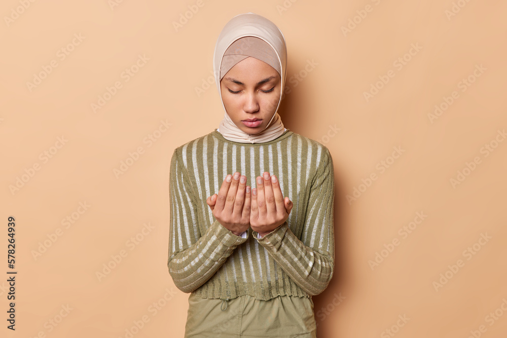 Muslim woman keeps palms together poses in praying pose keeps eyes ...