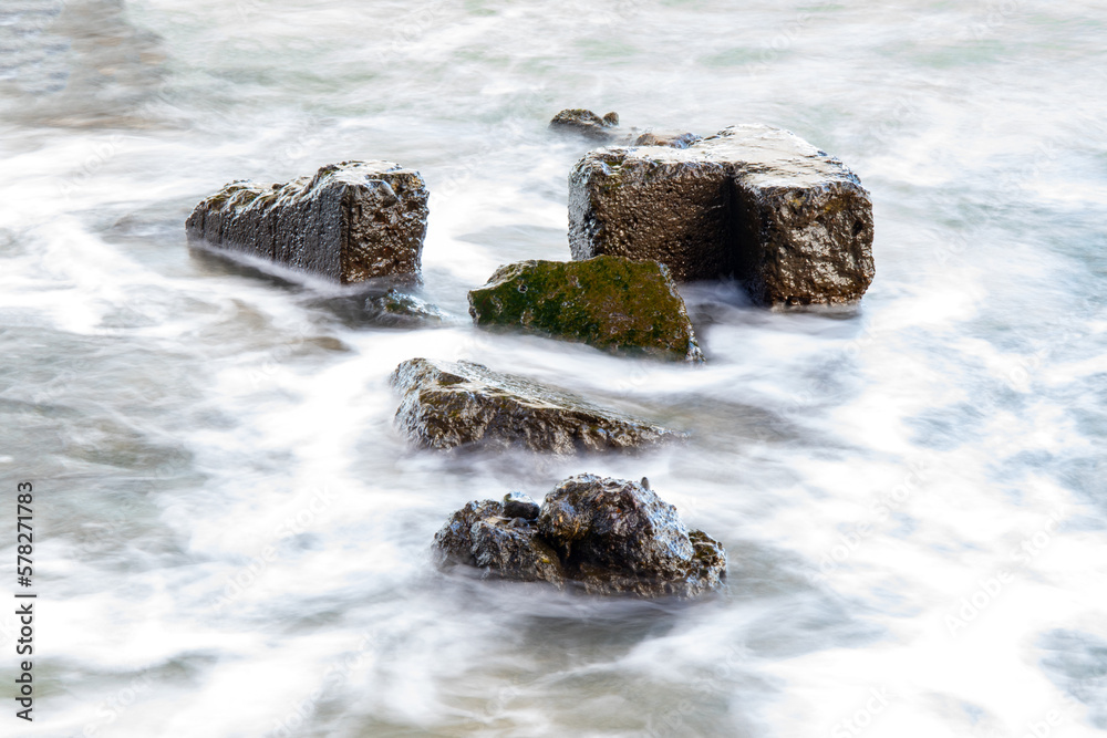 A long exposure photo of stones in the sea near the shore with ...