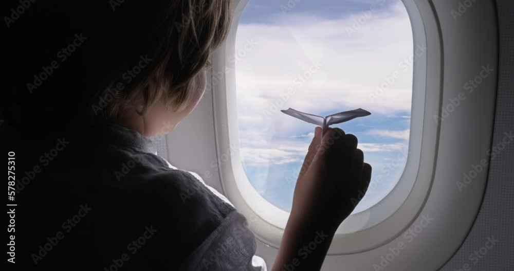 Back view, boy on plane looks dreamily out window and plays with paper ...