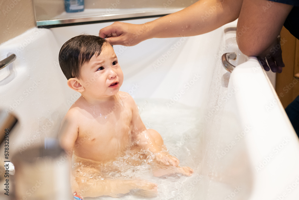 An unrecognizable new dad washing and giving his multiracial Asian male ...