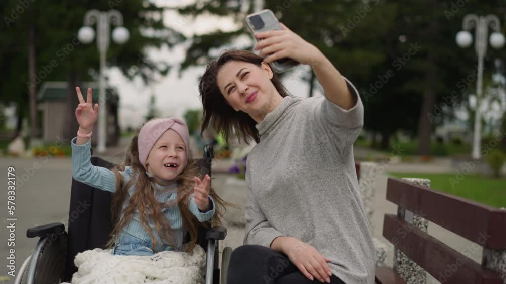 Mamma takes selfies while little girl with disability making funny gestures with hands. Woman ...