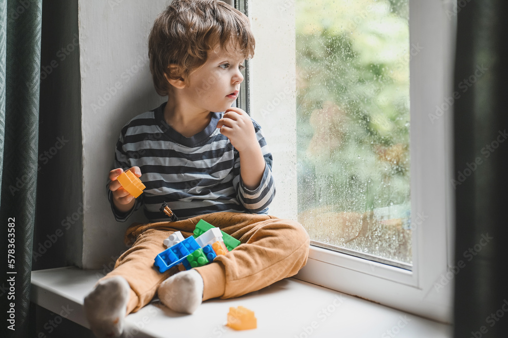 Little boy sitting on the window sill and playing with lots of colorful ...