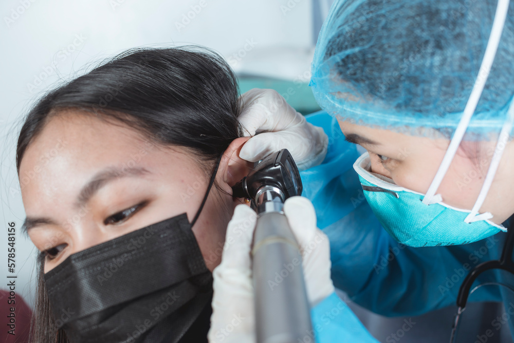 A doctor in full PPE gear checks the ear drum of a female patient with ...