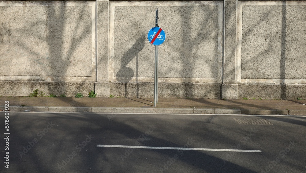 Cycle path end sign on a pole in the sidewalk. Rough concrete wall on ...