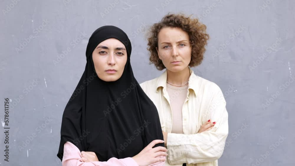 Two women stand with their hands folded, stare into camera. Portrait of ...