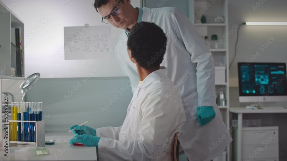 Two diverse male scientists in white lab coats working together in contemporary research ...