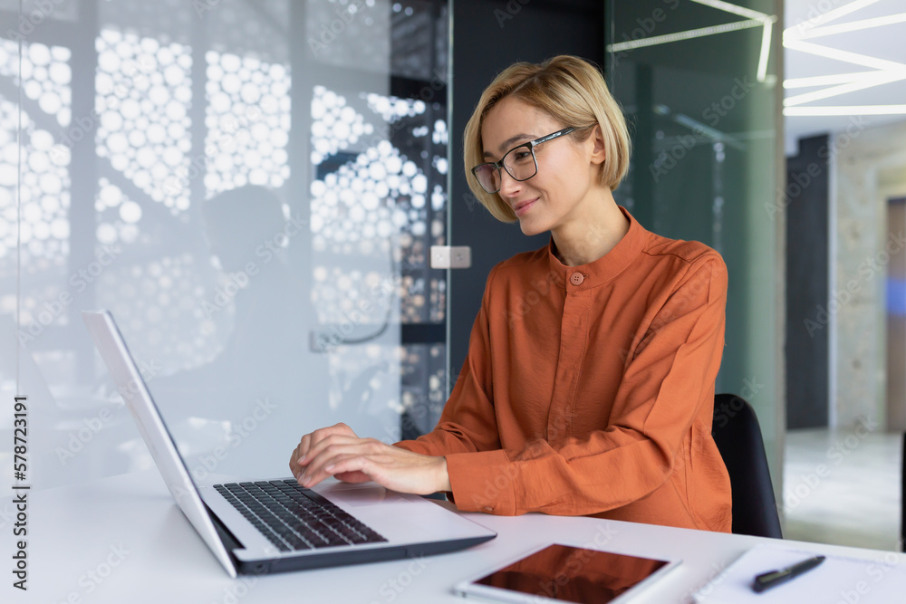 Beautiful young businesswoman inside office working with laptop, blonde ...