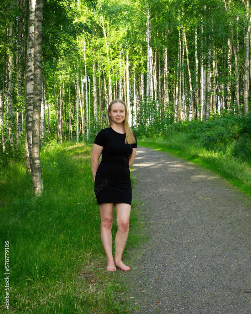 Young woman standing on a forest path. Wearing black dress and bare ...