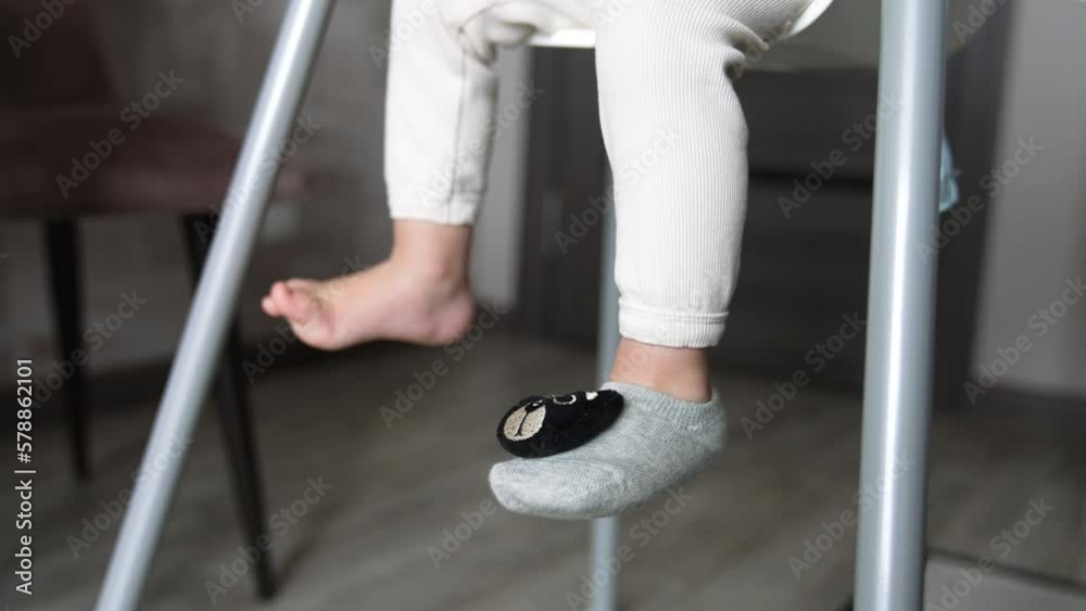 Adorable feet of a little baby sitting on the chair. One foot is bare ...