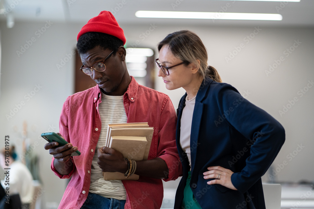 Two diverse students using mobile phone scrolling social media during ...