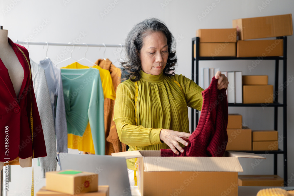 Elderly woman packing a shirt into a parcel box following an order, she ...