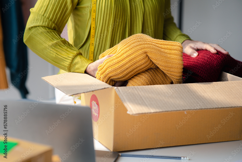 Elderly woman packing a shirt into a parcel box following an order, she ...
