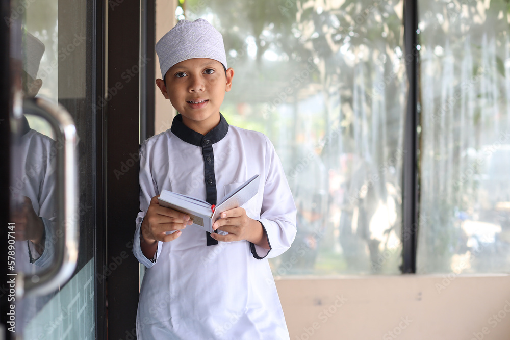 Smiling Asian muslim boy wearing muslim rob and skullcap with Quran ...