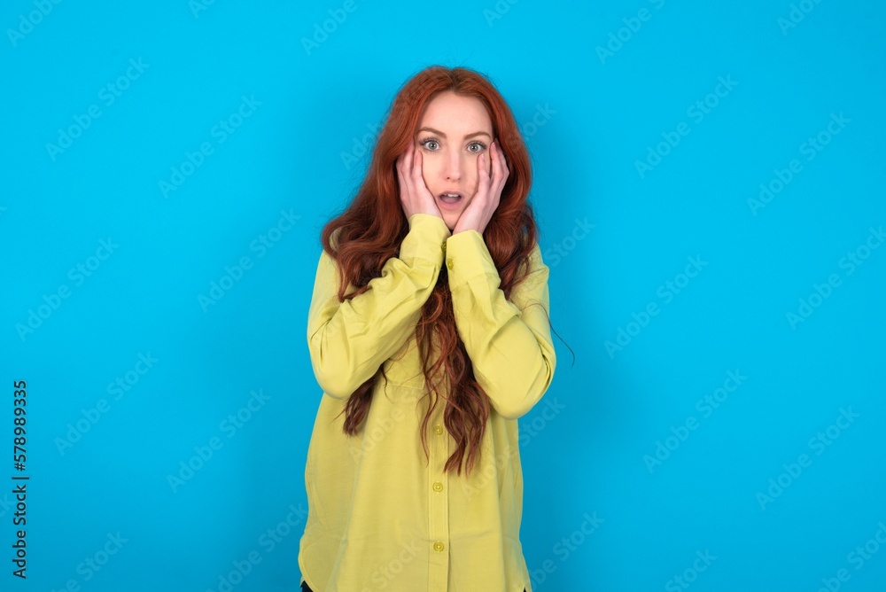 Stupefied young woman wearing green sweater over blue background ...
