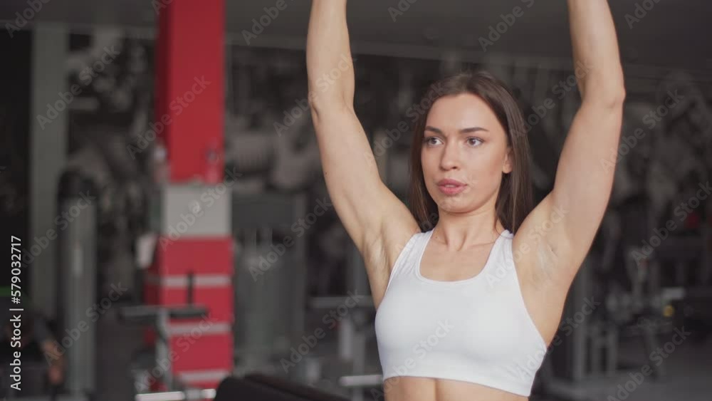 Beautiful woman lifts dumbbells and breaths during shoulder training ...