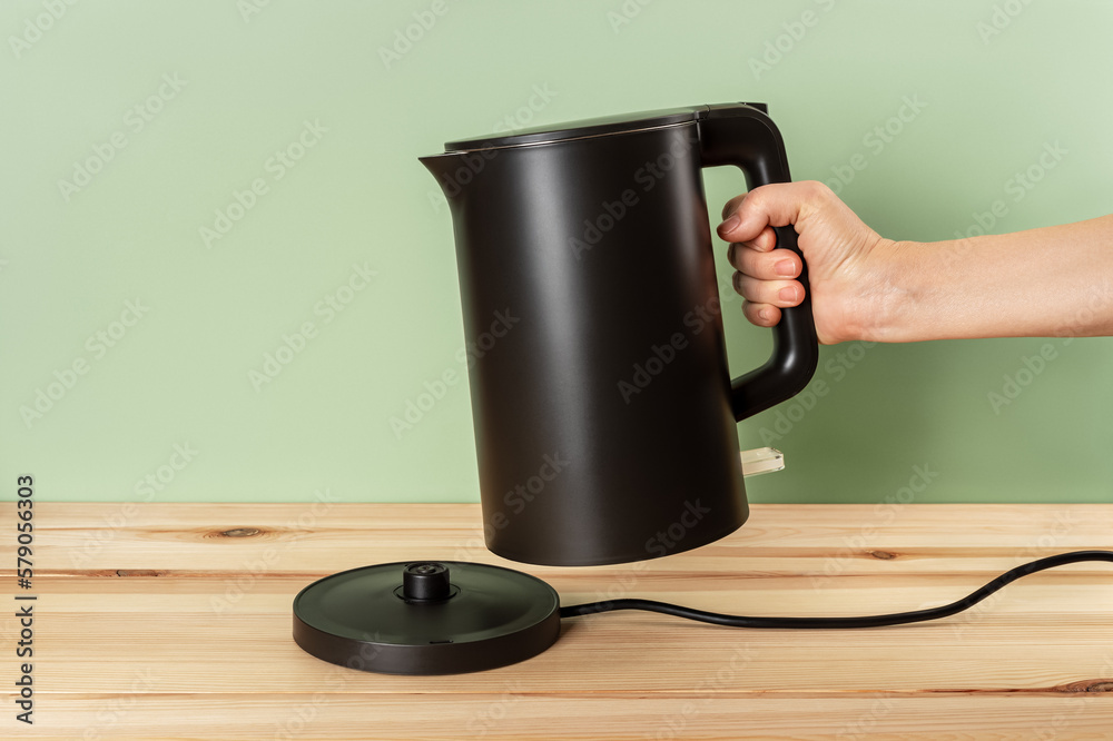 Matte black kettle kettle in a woman hand. Person hand taking off ...