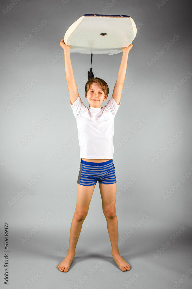 Smiling boy in striped swim trunks holding his boogie board above his ...