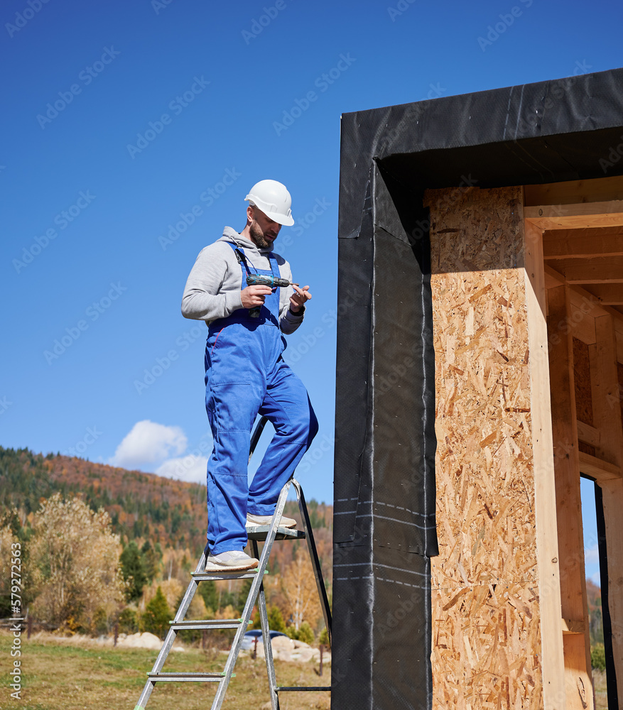 Male builder installing black corrugated iron sheet used as facade of ...