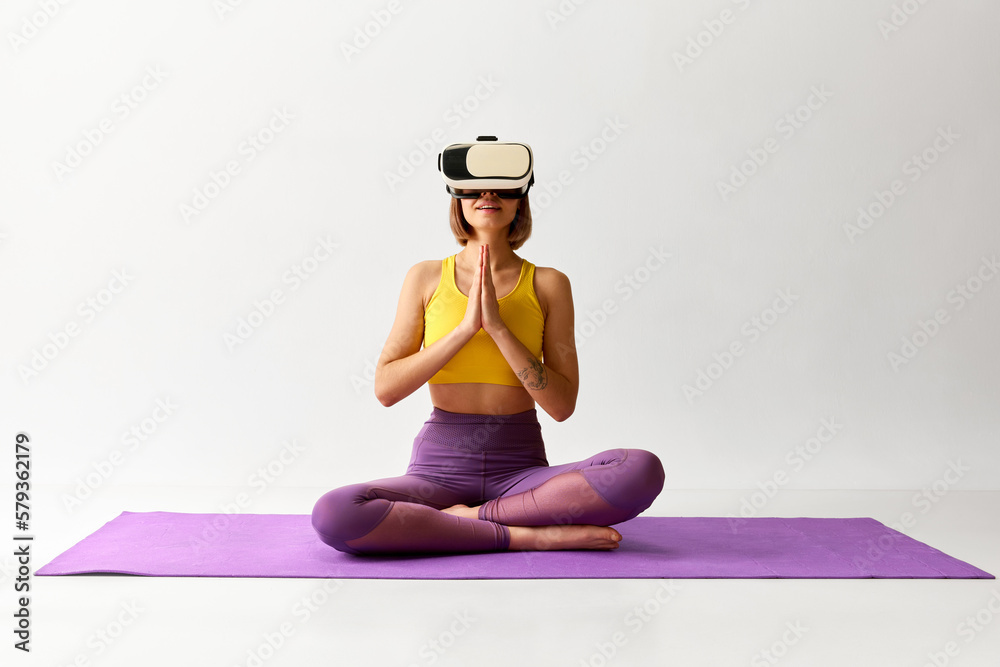 Flexible sportive young girl doing yoga exercises in VR headset glasses ...