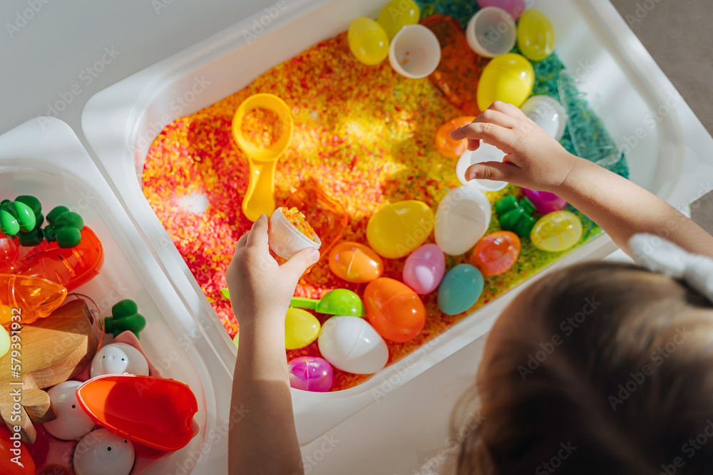 Child playing with colored rice and Easter eggs in sensory bin. Easter ...